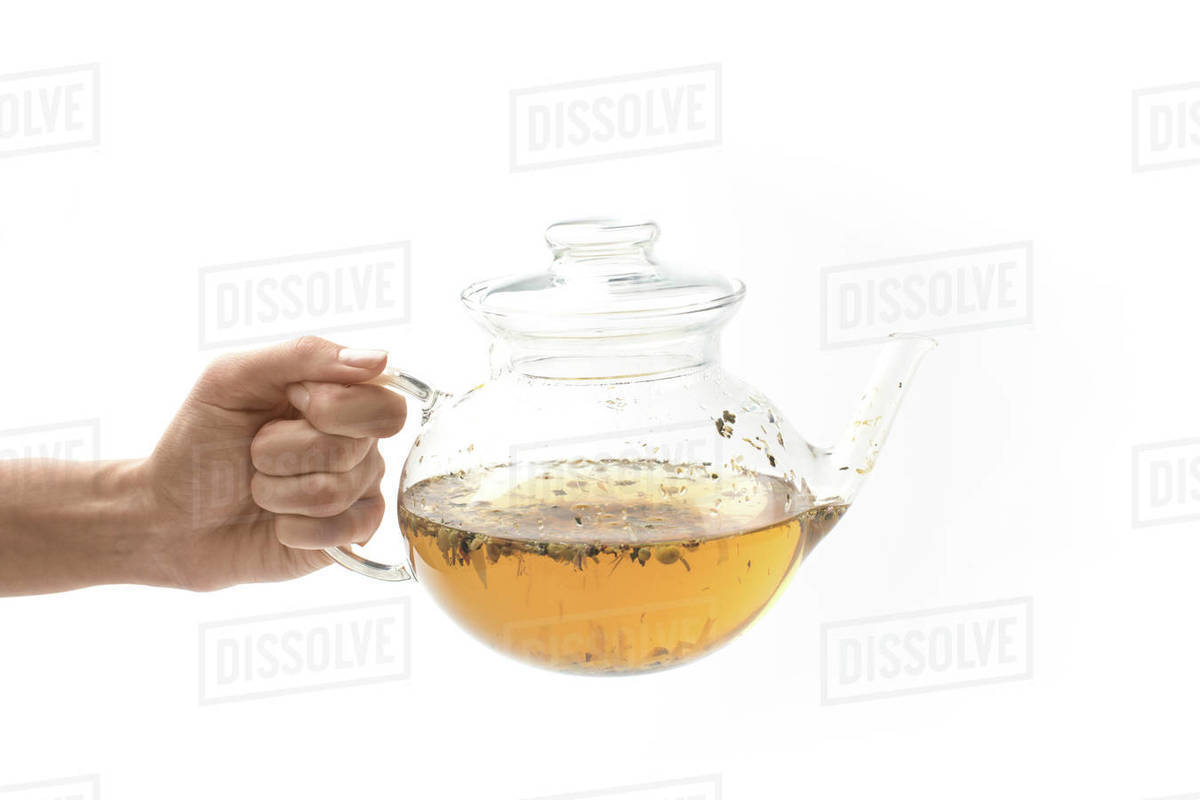 Close-up partial view of hand holding glass teapot with herbal tea ...