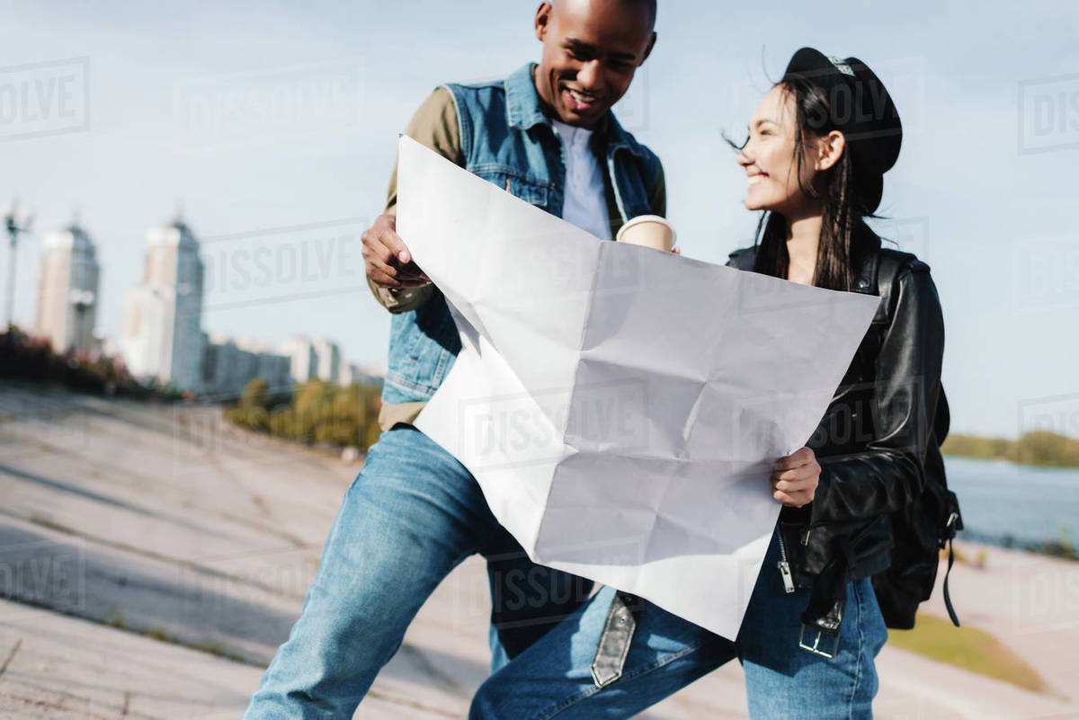 Portrait of multicultural couple with map in hands standing on street ...