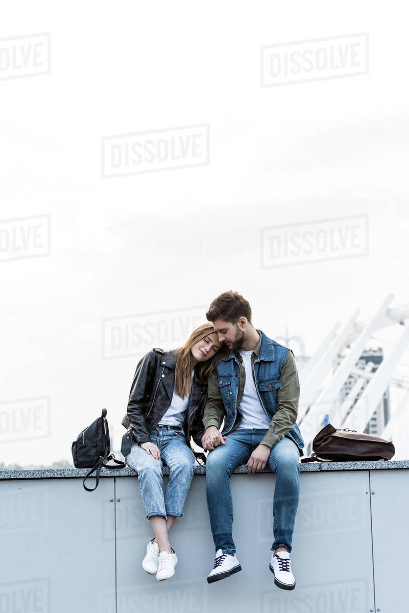 Young couple holding hands while resting on parapet together - Royalty-free Stock Photo | Dissolve