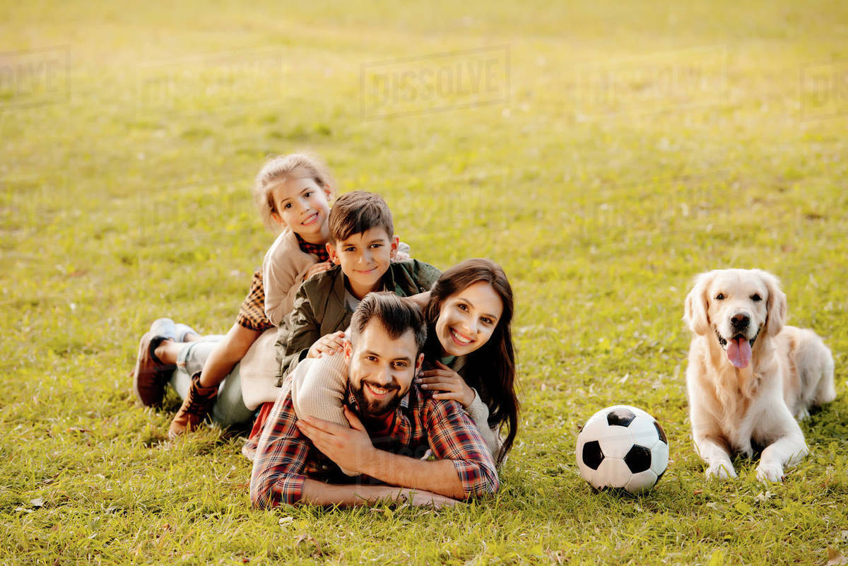 Happy family with two children lying in a pile on grass with dog ...
