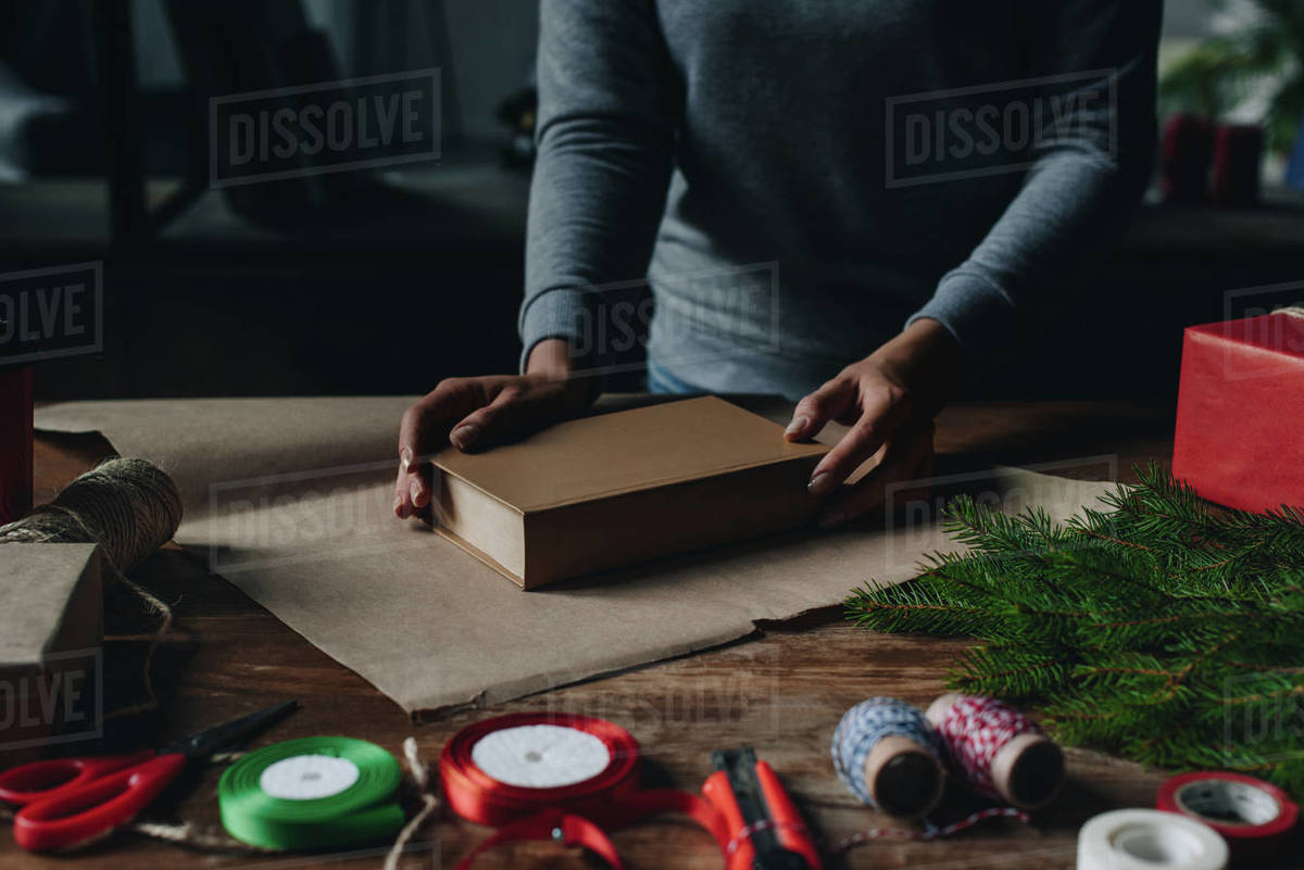 Cropped shot of woman wrapping book in craft paper as christmas gift ...