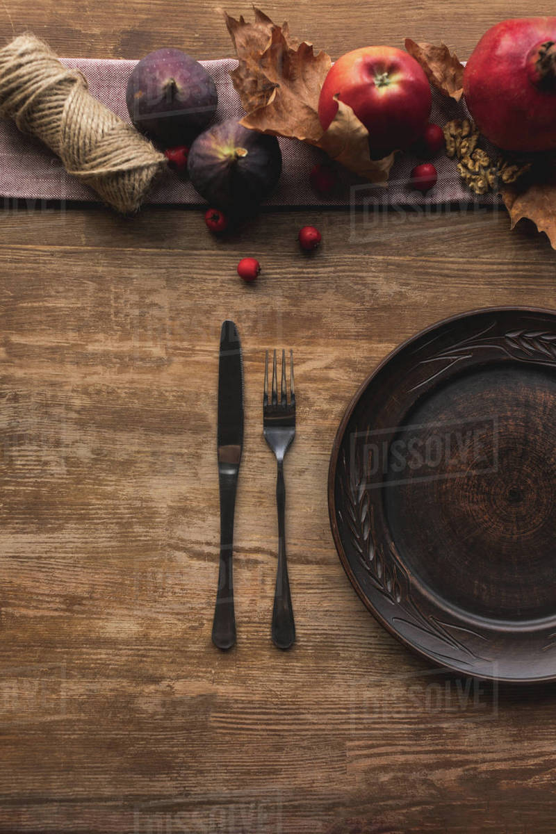 top view of empty plate with fork and knife, rope and ripe fruits on ...