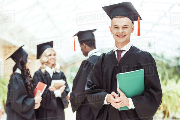 handsome young student in graduation costume with blurred multiethnic ...