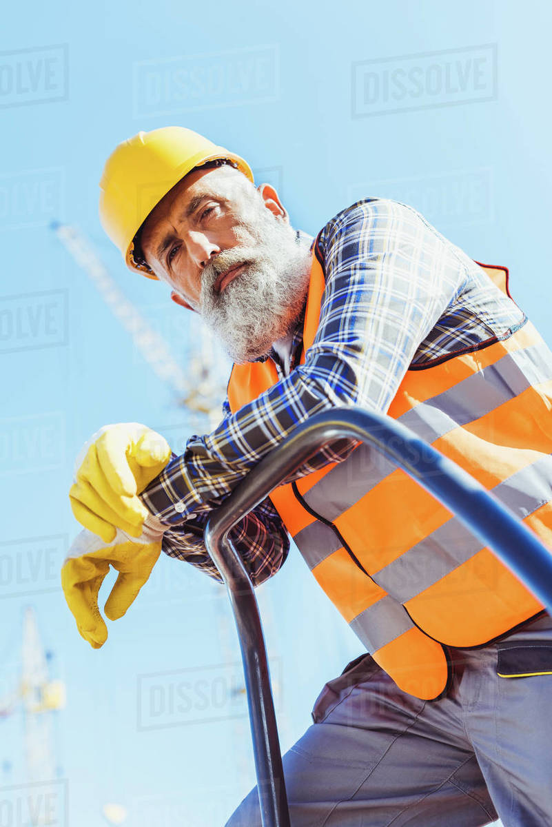 Bearded construction worker in reflective vest and hardhat leaning on ...