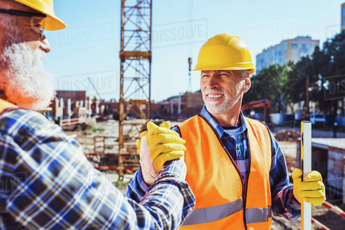 Smiling construction worker in protective uniform shaking hands with ...