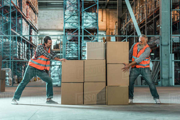Warehouse workers moving boxes while working together in storehouse ...