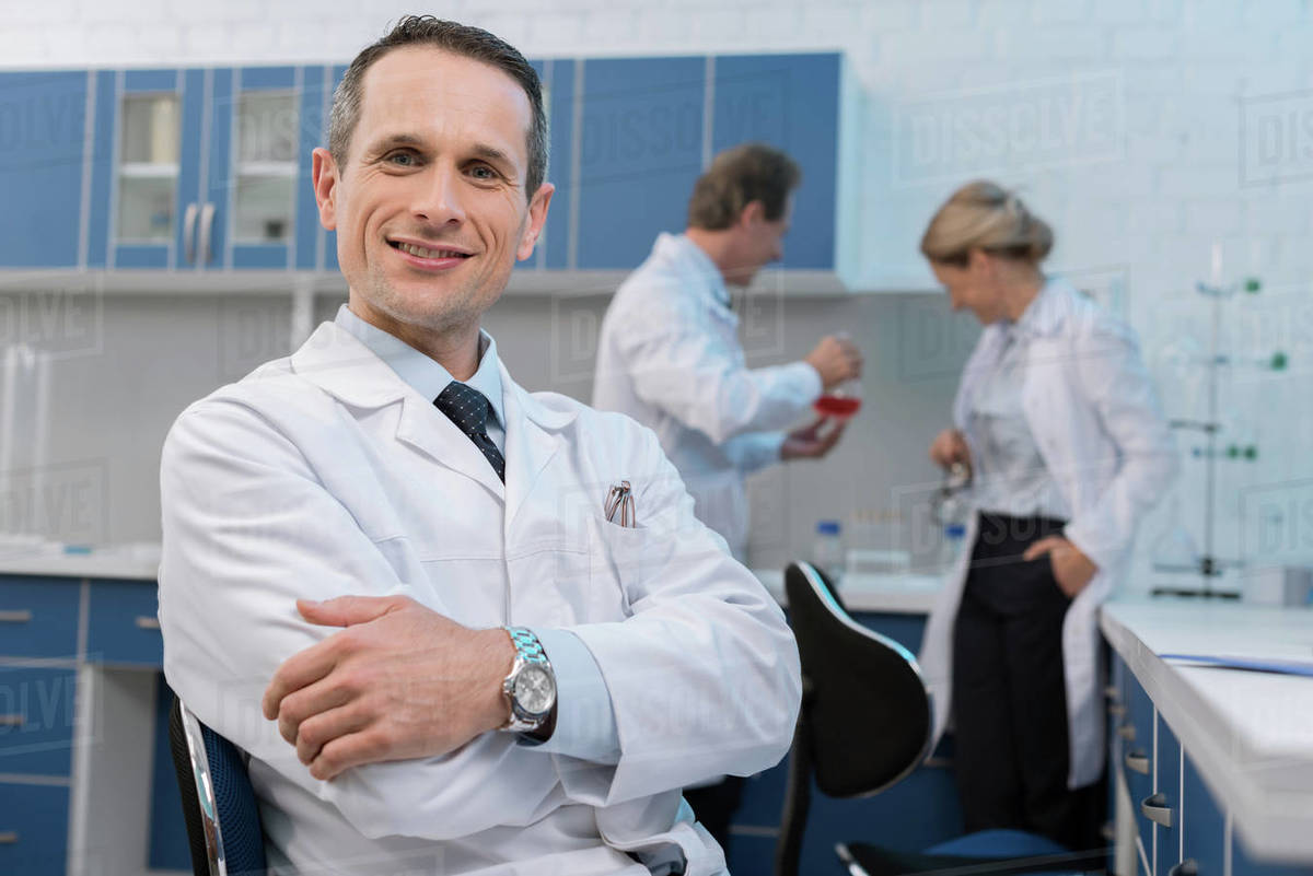 Smiling medical worker in laboratory, sitting with arms crossed and ...