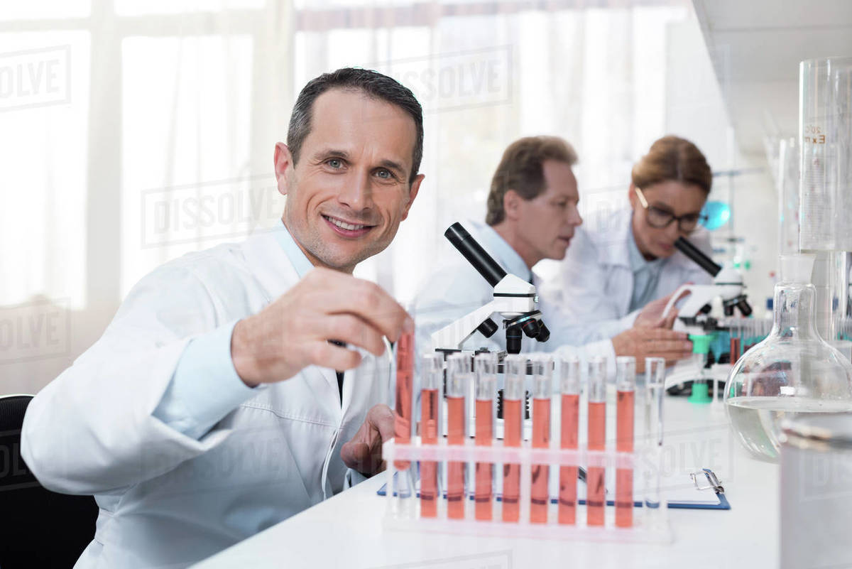 Smiling male scientist in white coat holding a test tube with red ...