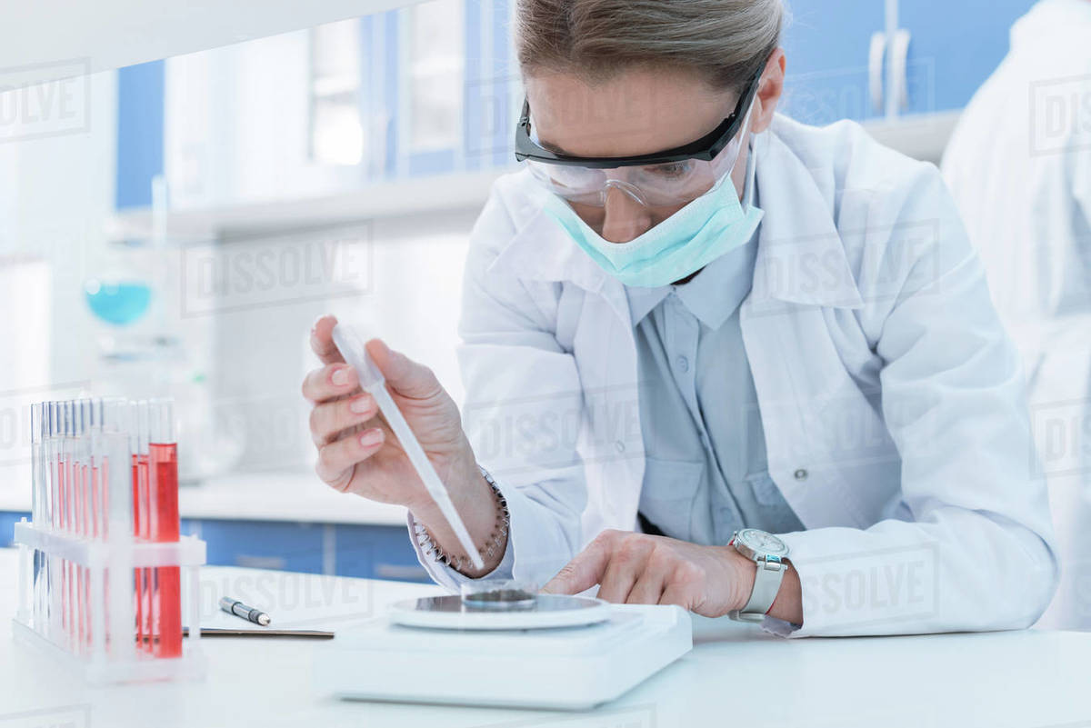 Professional scientist in sterile mask and protective glasses, making ...