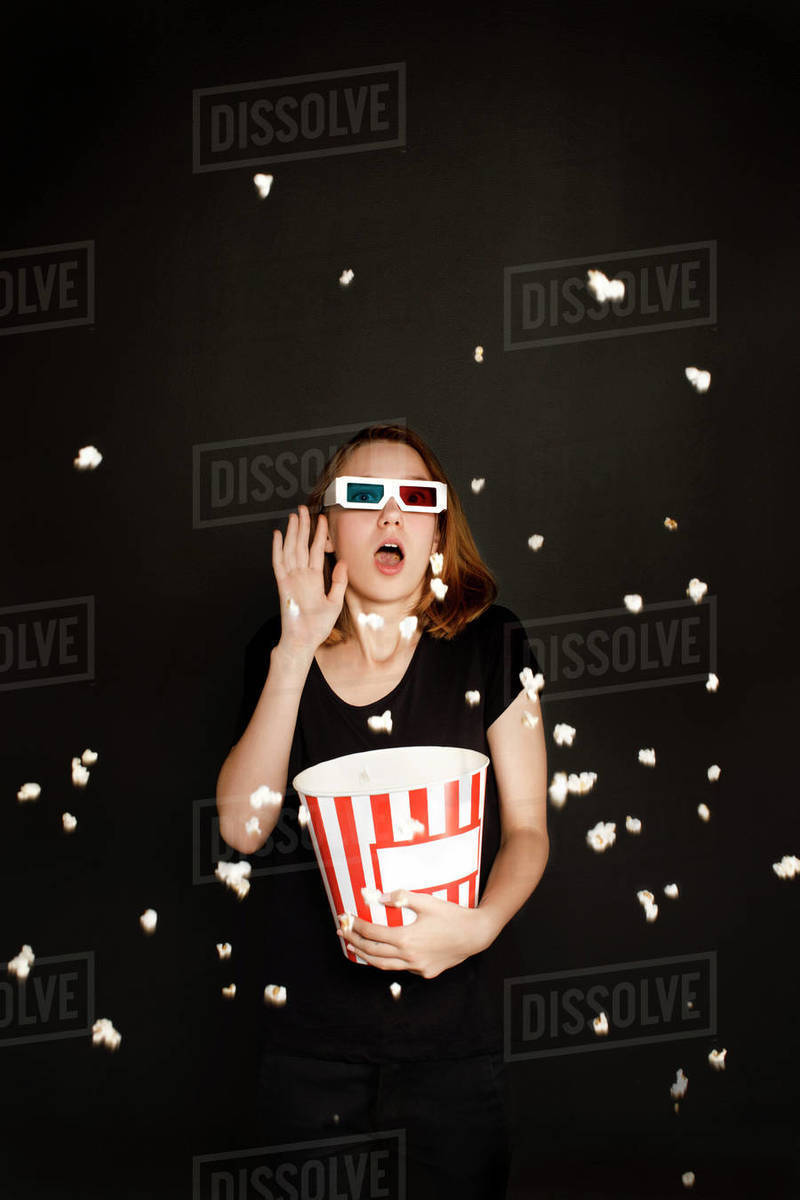 Shocked young woman with bucket of popcorn isolated on black - Royalty ...
