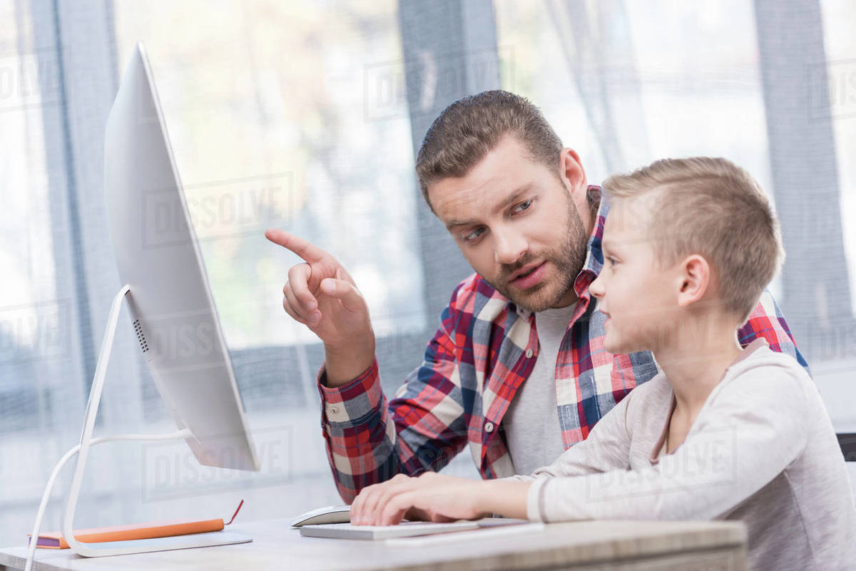 Concentrated father and son using desktop computer and pointing at screen - Stock Photo - Dissolve