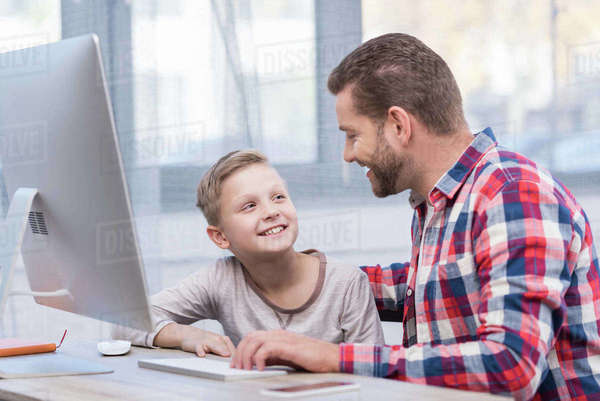 Happy father and son using desktop computer and smiling each other ...