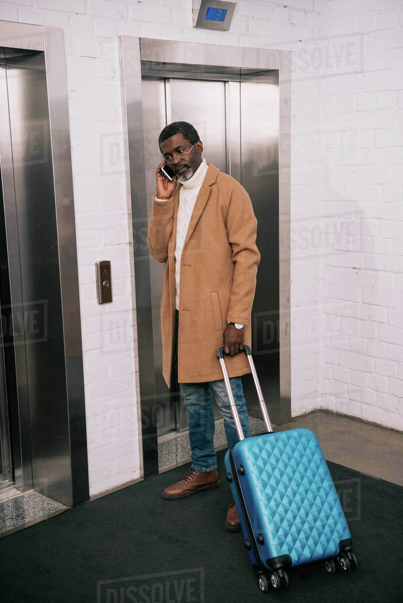 Middle aged man waiting for lift standing with wheeled bag - Royalty ...