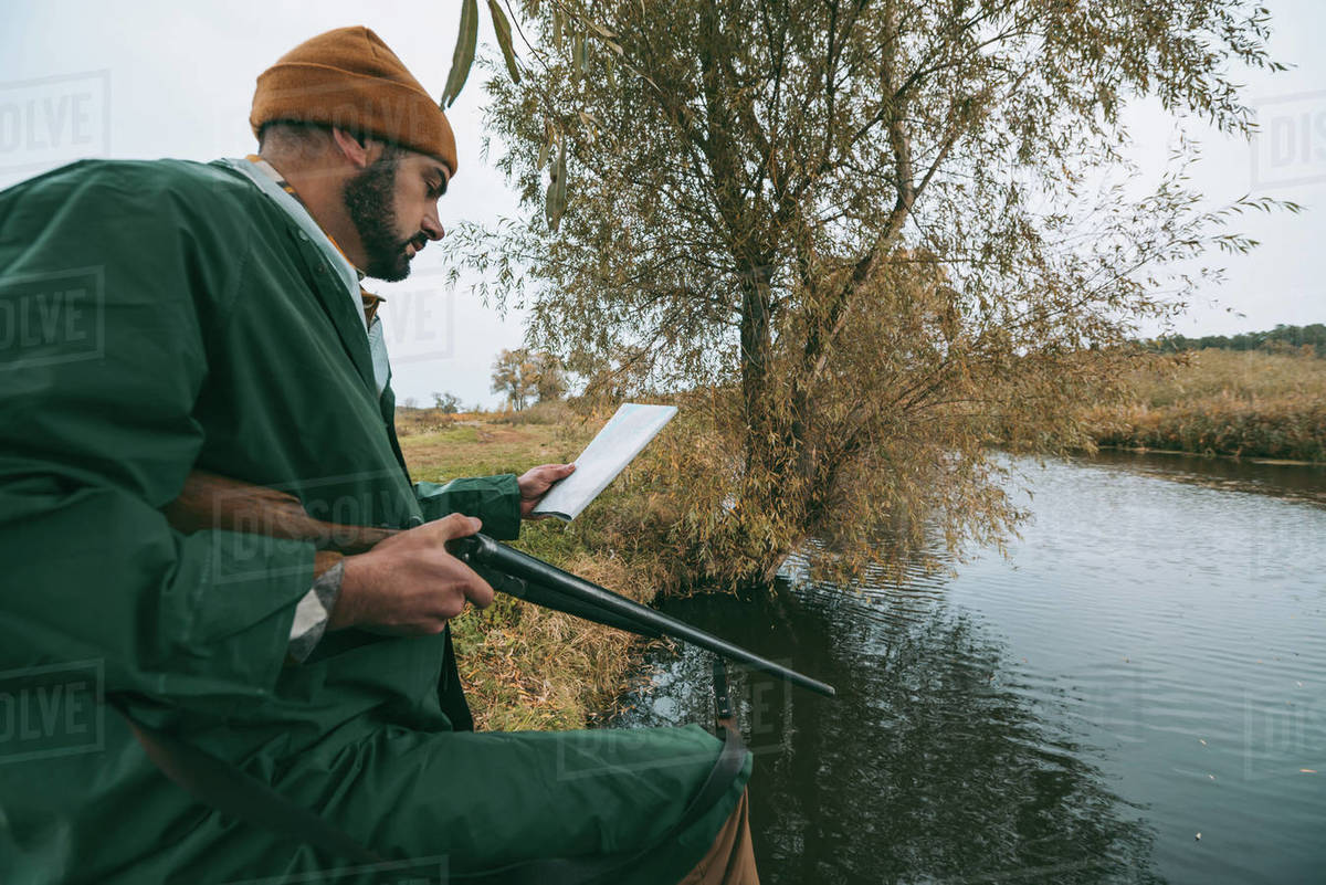 Handsome hunter standing with a gun and looking at map - Royalty-free ...