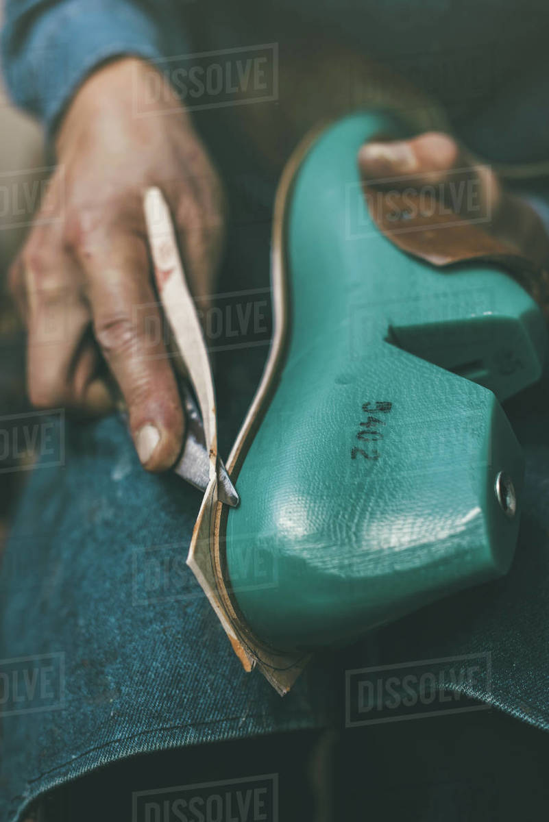 Cropped shot of shoemaker cutting material with knife to size of foot ...
