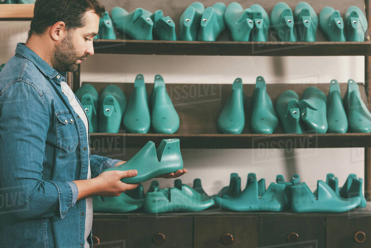 Side view of bearded shoemaker holding footwear workpiece at workshop ...