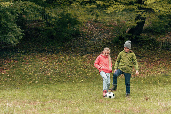 full length view of cute little kids playing soccer in autumn park ...