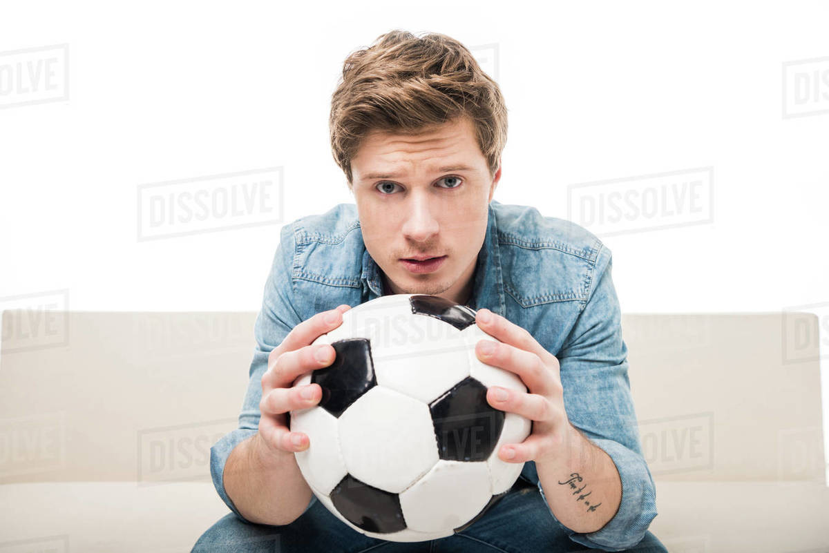 Emotional young man holding soccer ball and looking at camera isolated ...