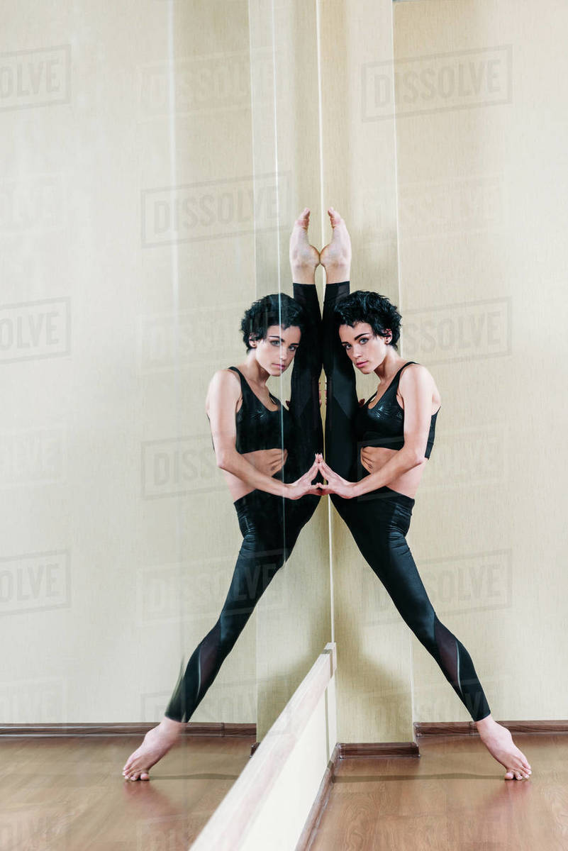 Young sportive woman doing stand split at mirror in dance studio and ...