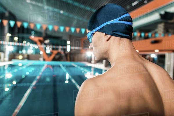 Back view of muscular swimmer in swimming cap and goggles standing at ...