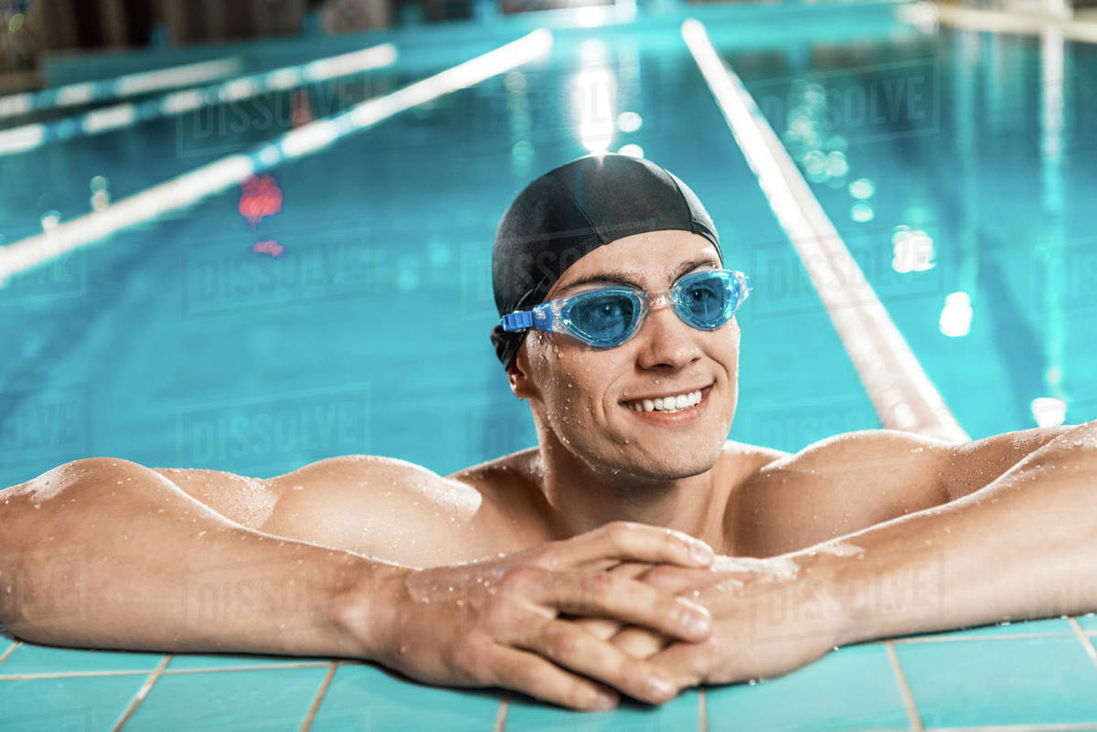 Handsome muscular swimmer in swimming cap and goggles in swimming pool ...