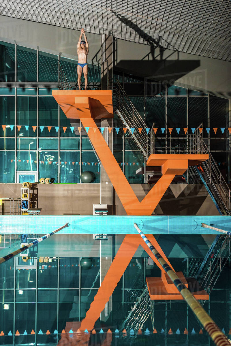 Swimmer standing on diving platform ready to jump at swimming pool ...