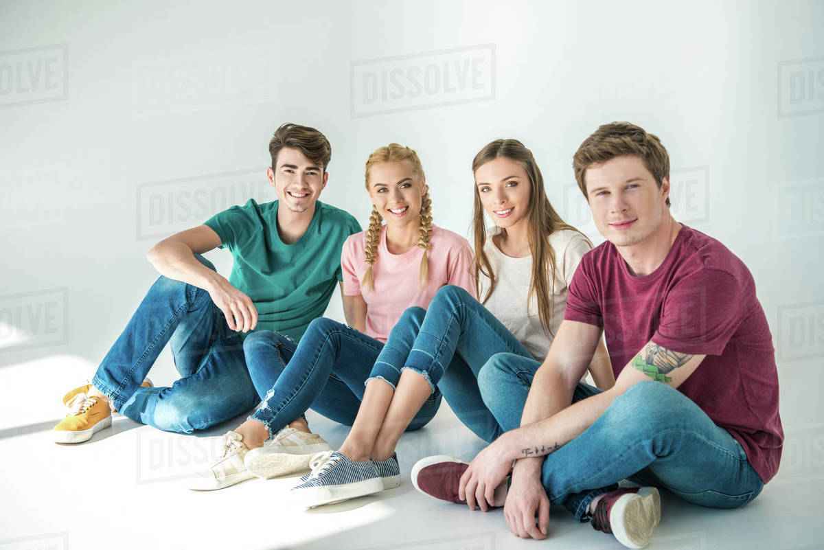 Happy young friends sitting together and smiling at camera on grey ...
