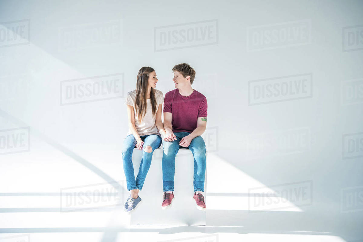Happy young couple sitting together and smiling each other on grey ...