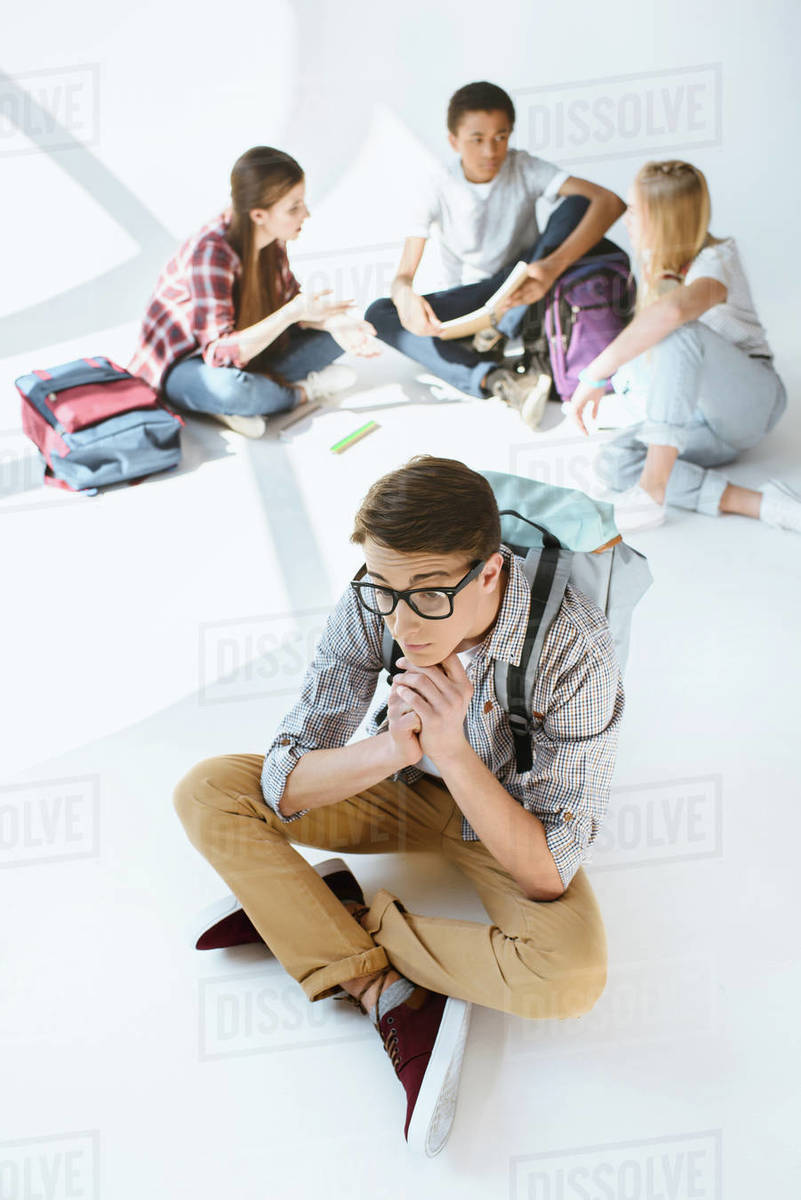 Teenage boy sitting alone while multicultural group of students resting ...