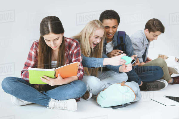 Students doing homework while multiethnic friends using smartphones ...
