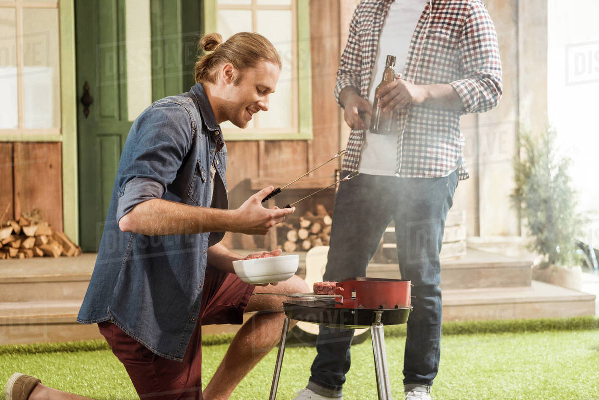 Two men grilling burgers while drinking beer together outdoors ...