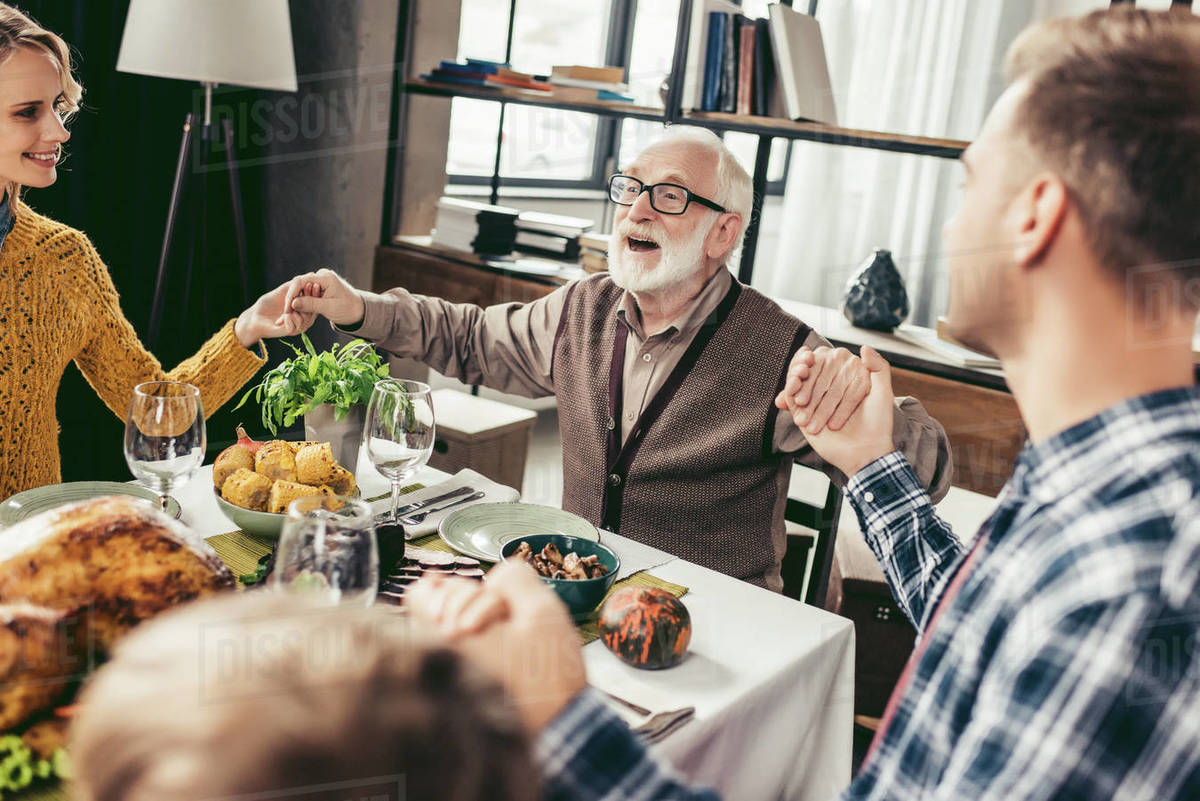 Happy Christian family praying before holiday dinner and holding hands ...