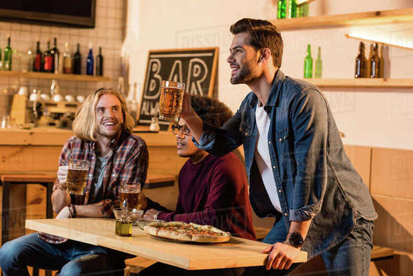 Smiling young multiethnic friends drinking beer together in bar ...