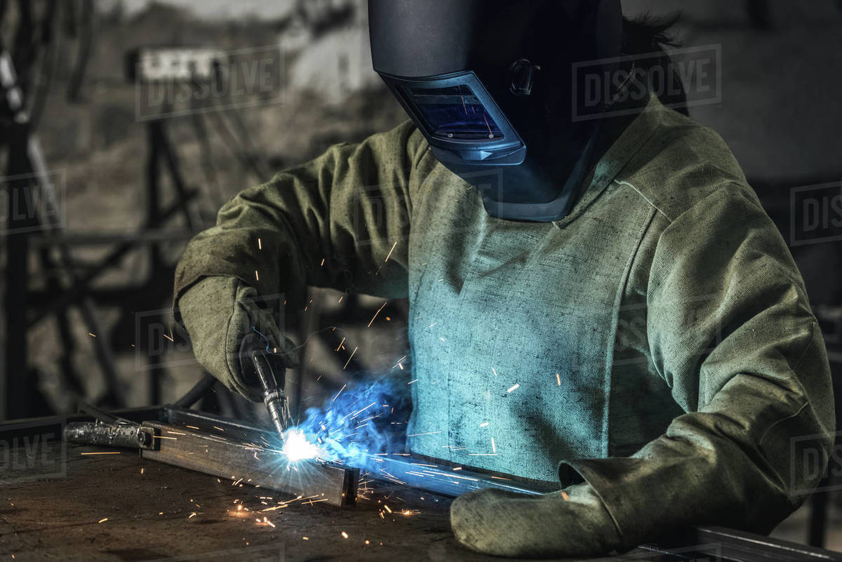 Manual worker in protective helmet with welding torch working in ...