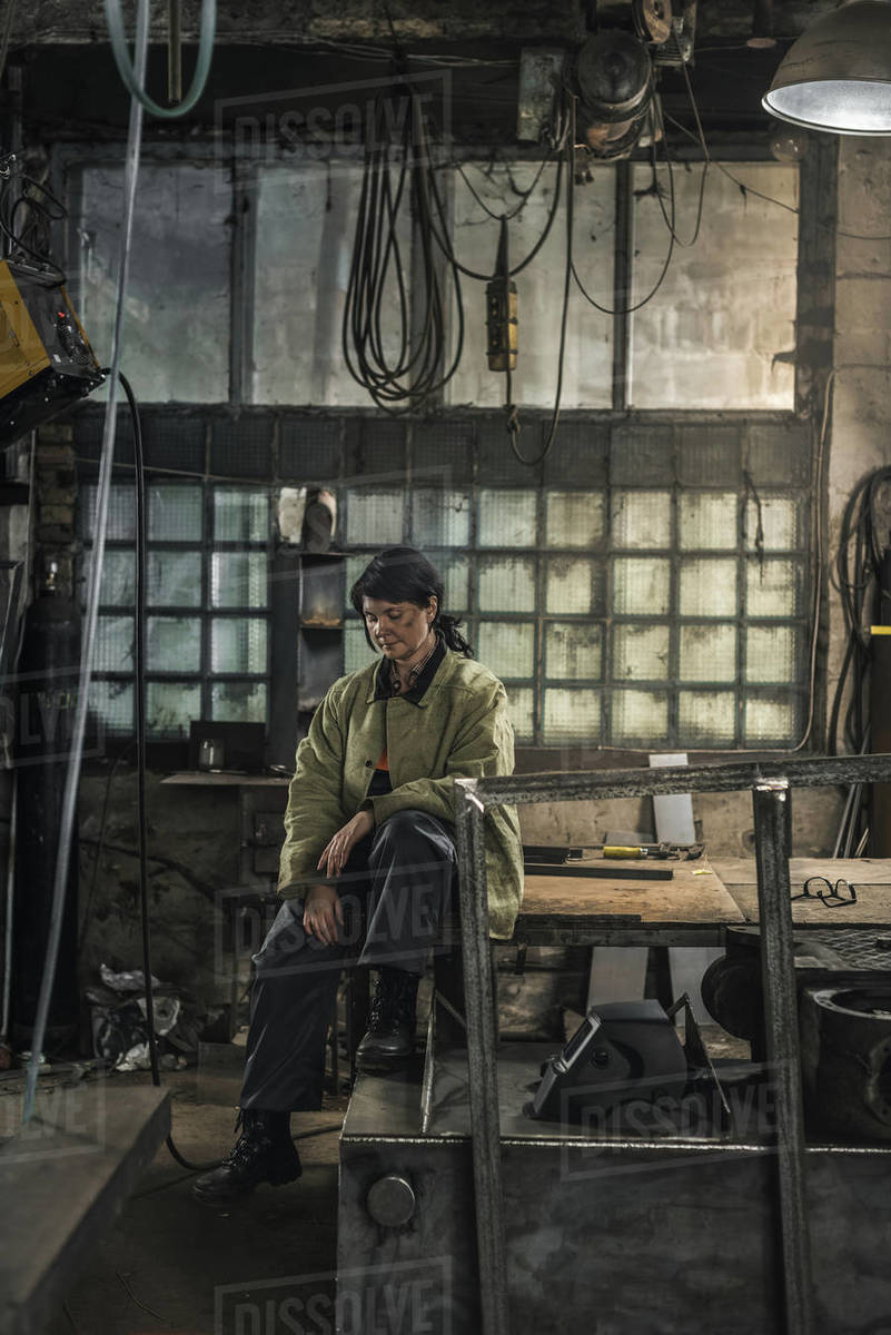 Tired female welder sitting on table while having rest during work ...