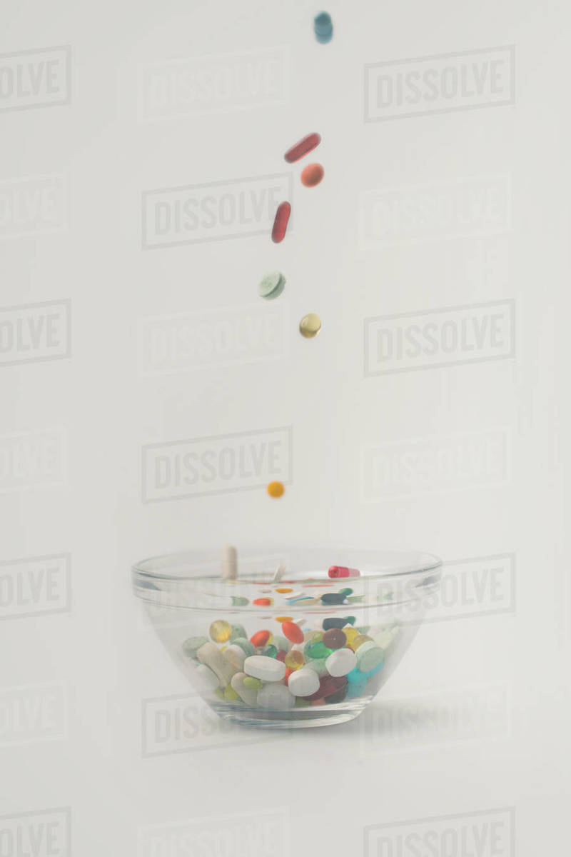 Pills falling into transparent glass bowl isolated on white - Royalty ...