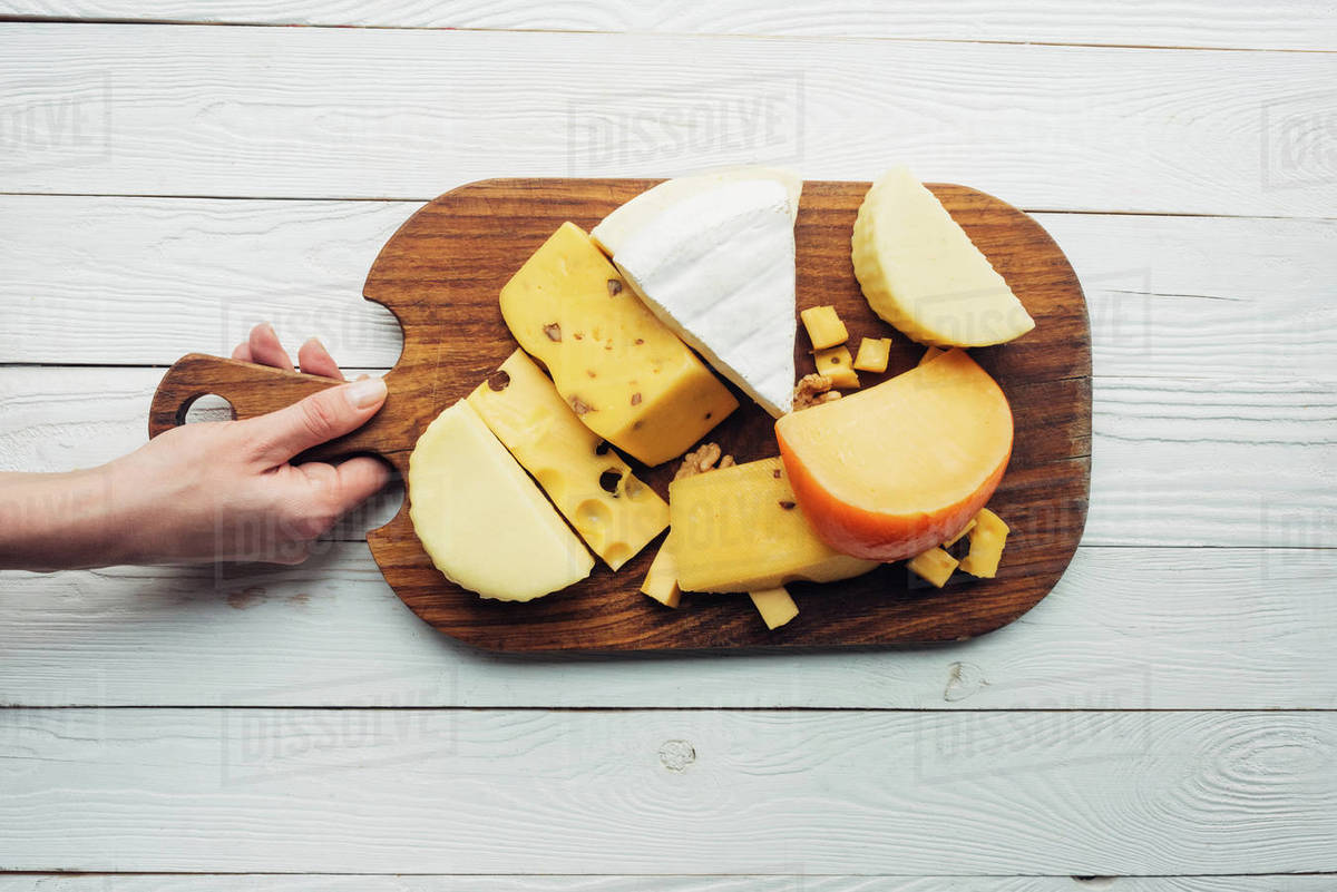 Top view of female hand holding assorted cheese on wooden cutting board ...
