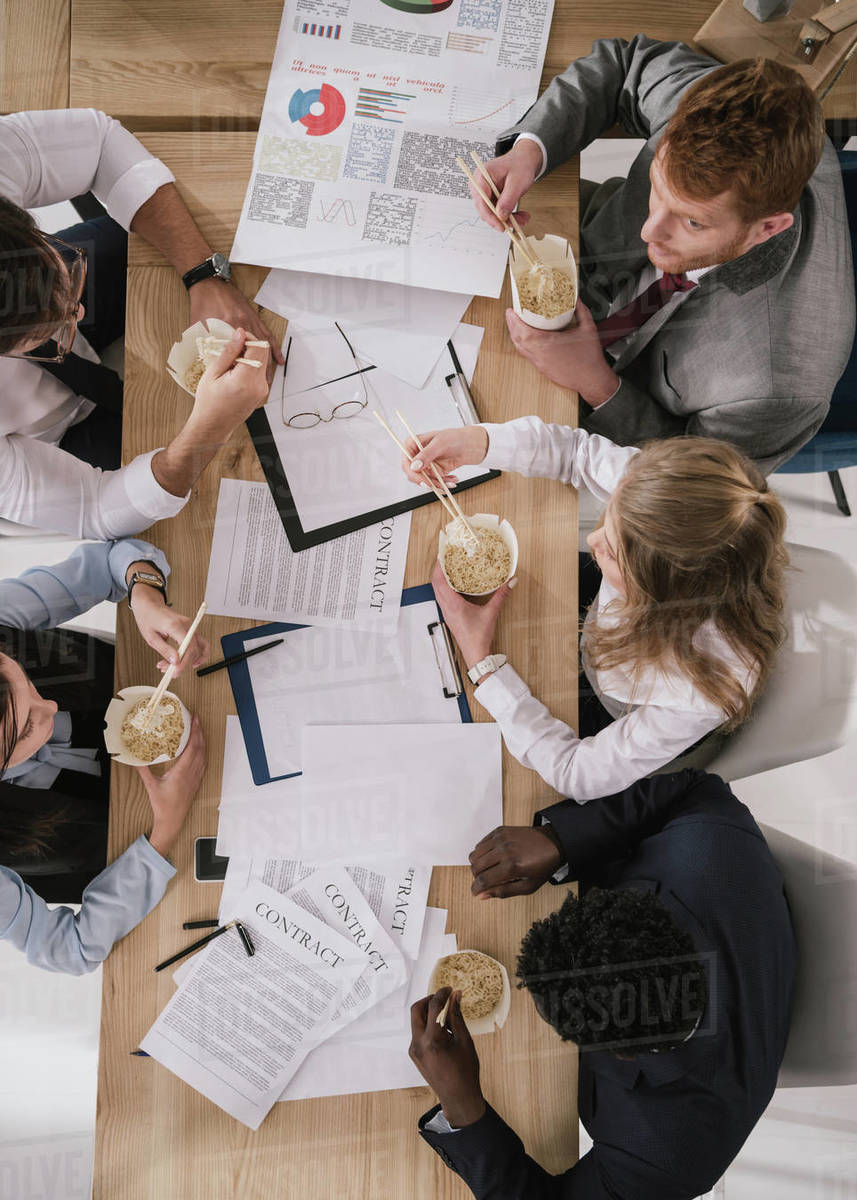top view of businesspeople eating noodles while having paperwork at ...