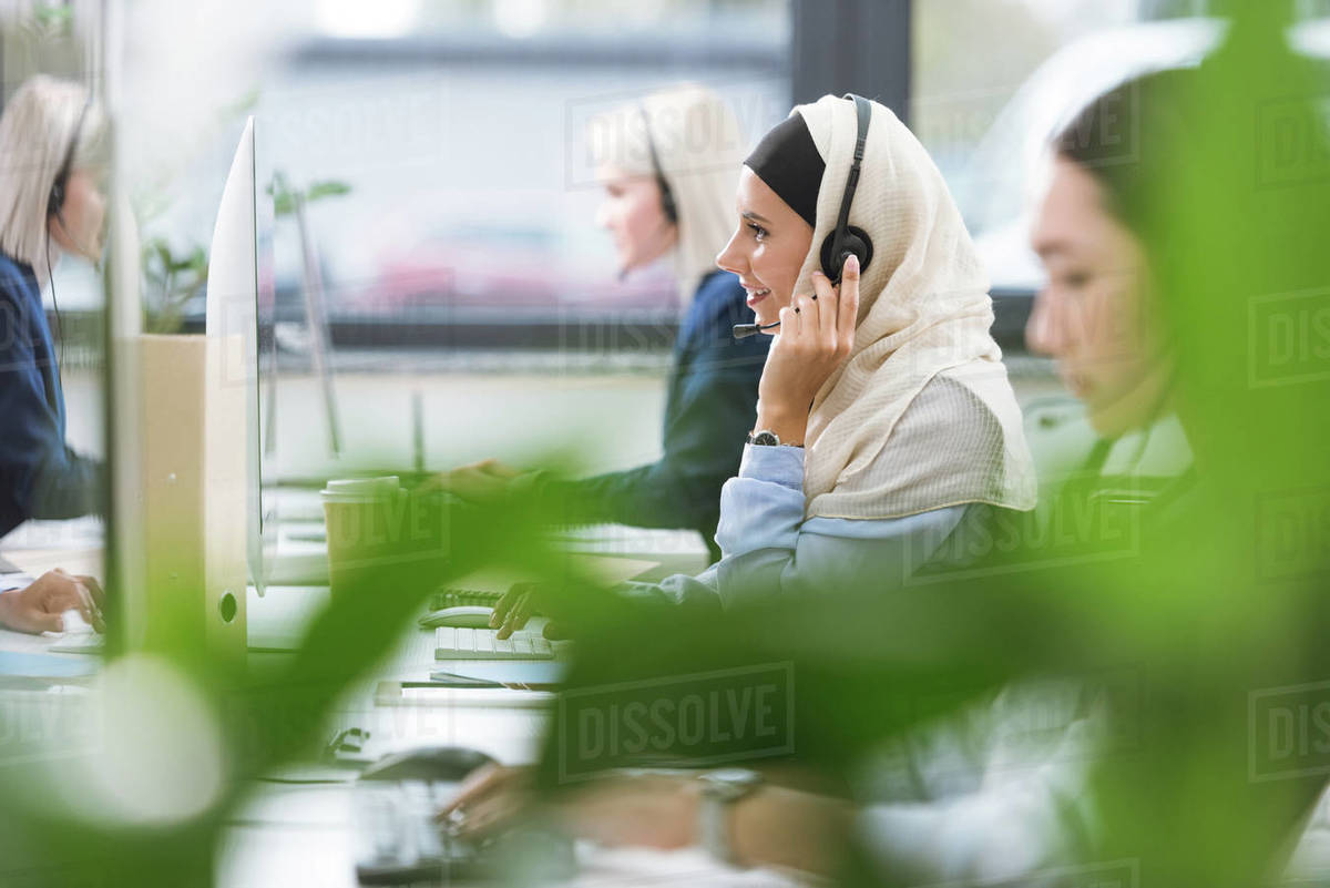 Selective focus of smiling arabic call center operator in hijab in ...