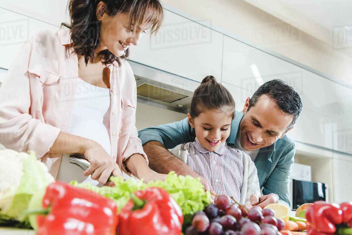 Cheerful family slicing fruits and vegetables together at kitchen ...