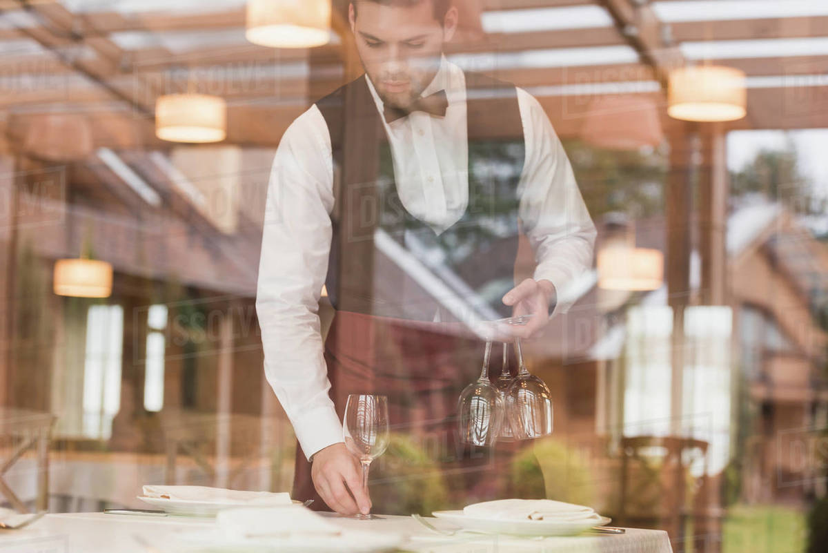View through the window on a waiter putting wineglasses on a table ...
