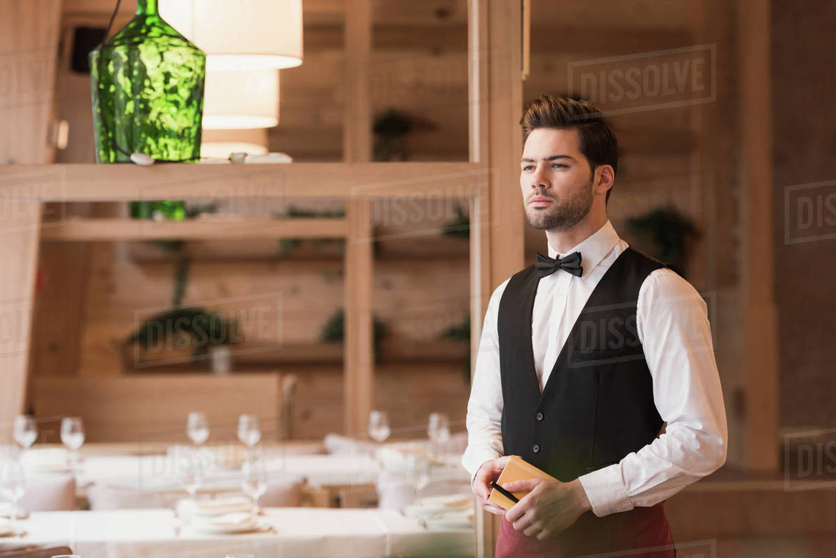 Waiter standing with notebook and pen and looking away - Royalty-free ...