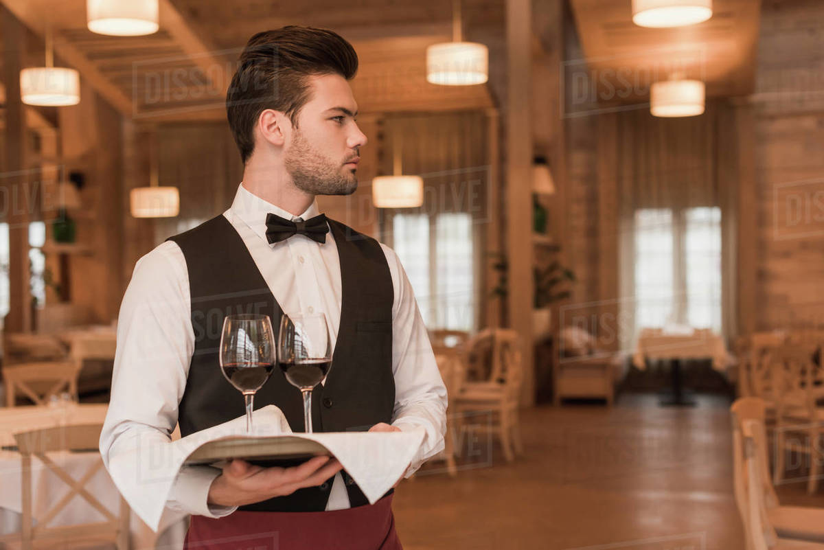 Waiter holding tray with glasses with red wine and looking away - Stock ...
