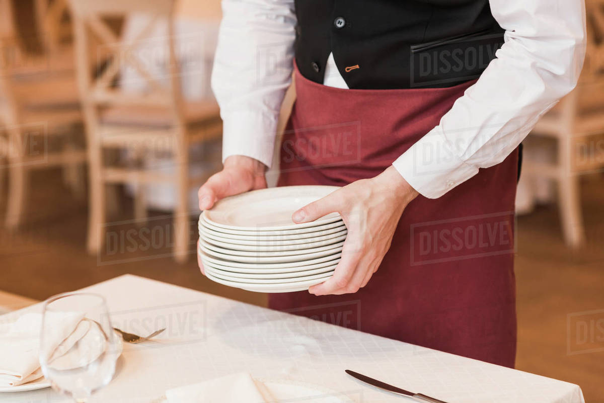 Cropped image of Waiter putting pile of plates on the table - Royalty ...