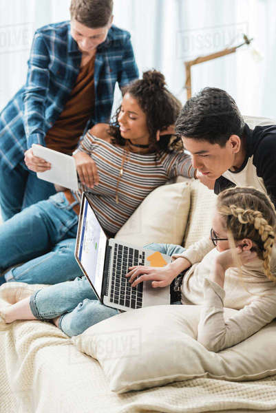 Smiling multicultural teenagers looking at laptop with loaded facebook ...
