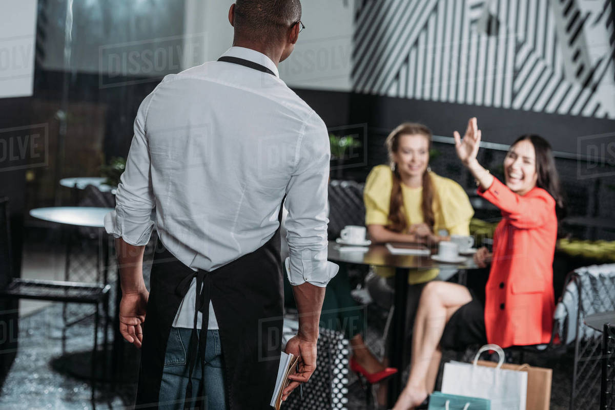 Happy young women waving to waiter at cafe - Stock Photo - Dissolve