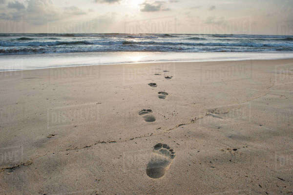 Footsteps on sandy beach moving into sea at sunset - Royalty-free Stock ...