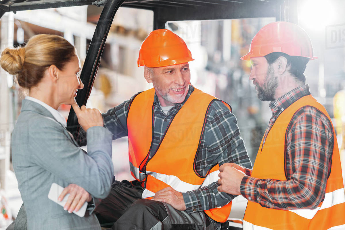 Two workers and inspector using forklift machine in storehouse - Stock ...