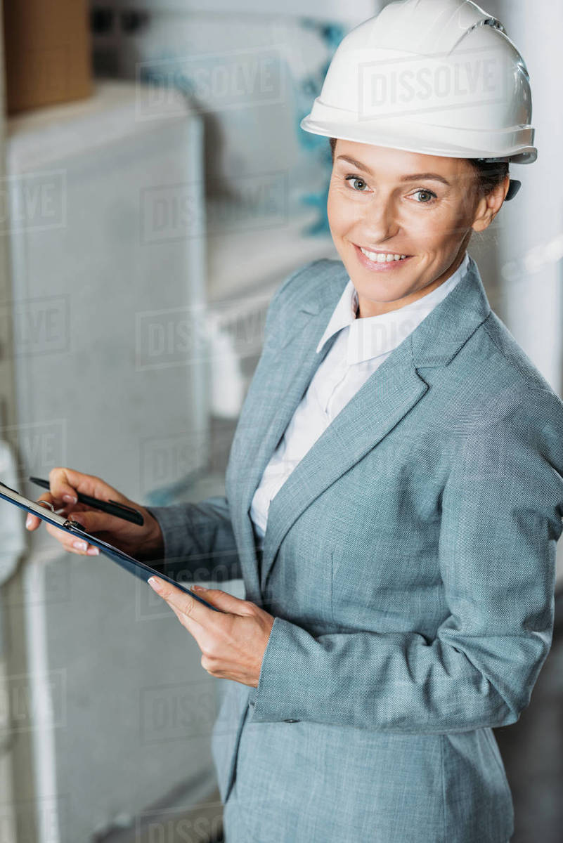 Female inspector in helmet writing notes on clipboard in warehouse ...