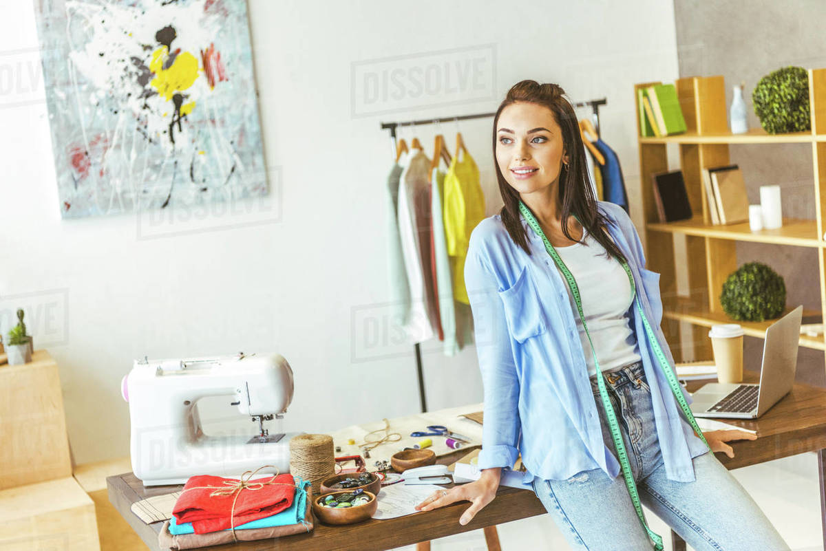 Smiling seamstress leaning on table and looking away - Royalty-free ...